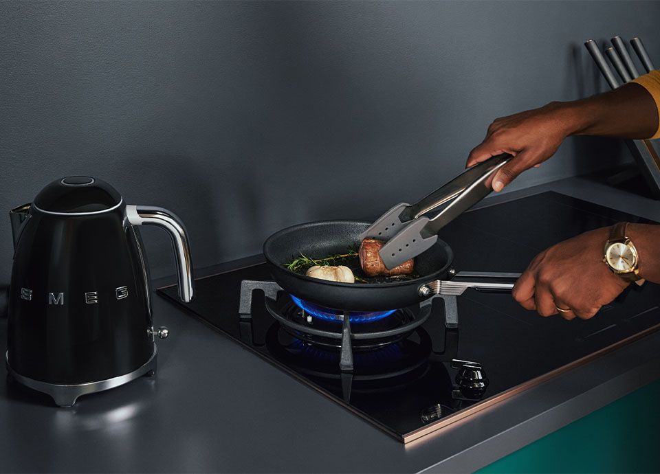 Man cooking steak on a gas Dolce Stil Novo cooktop with a Smeg Black Kettle